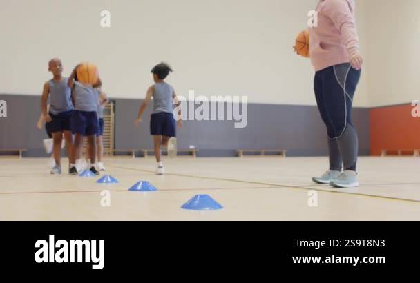 Dribbling basketball around cones, children practicing in school gym ...