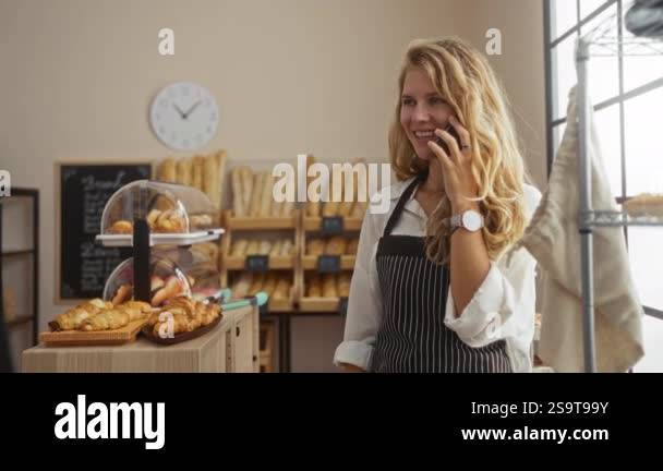 Young blonde woman in a bakery shop wearing an apron smiles while ...