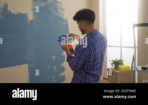 Young man selecting paint colors in living room of new home, holding ...