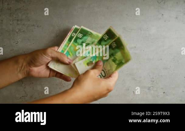 Hands counting israeli shekel banknotes against a concrete background ...