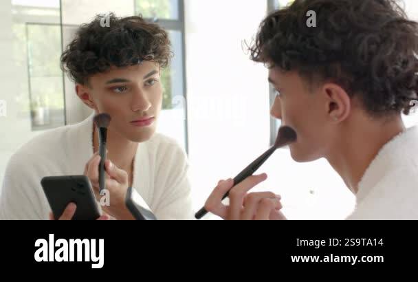 Applying makeup, young non binary person using brush and looking in mirror. Beauty, self-care ...