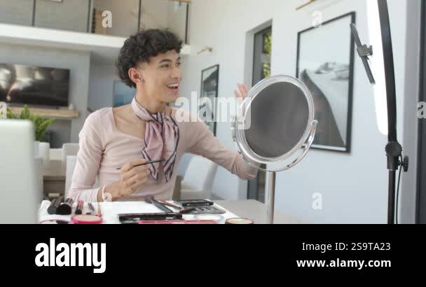 Applying makeup, non binary person smiling and using mirror in modern ...
