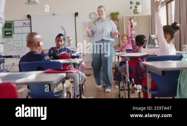 In school classroom, students raising hands while female teacher engaging with them. Education ...