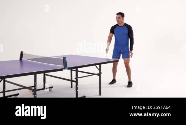 Playing table tennis, man hitting ball with paddle in studio setting ...