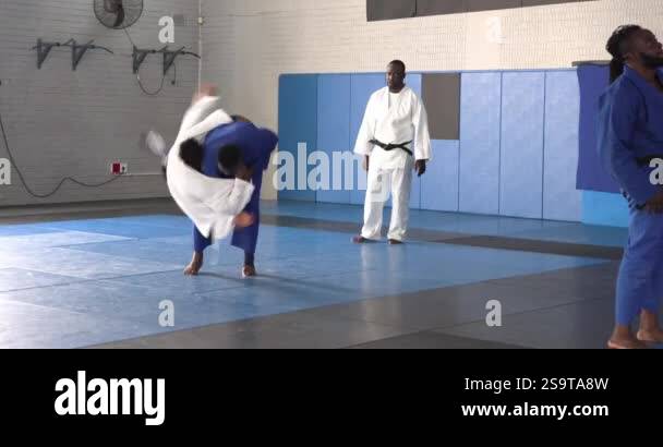 Practicing judo, two men sparring while instructor observes in dojo ...