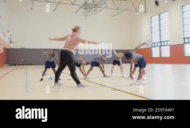 In school gym, students stretching with female teacher leading group ...