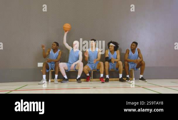 Basketball team sitting on bench, wearing uniforms, chatting and ...