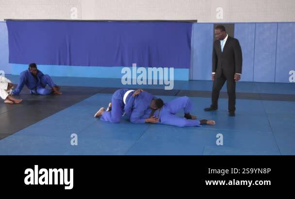 Practicing judo, athletes in blue uniforms grappling on mat with coach ...
