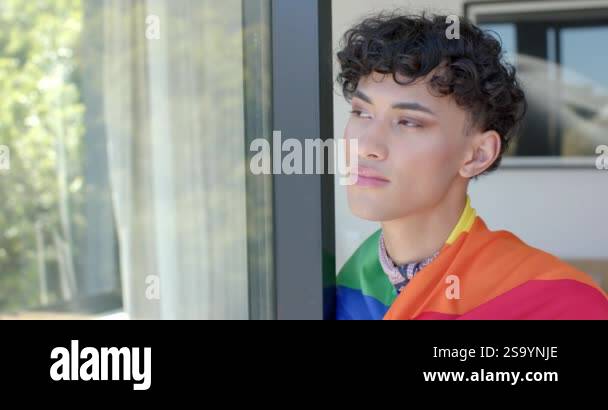 Looking out window, person wrapped in rainbow flag, contemplating ...