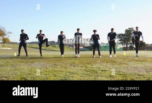 Cricket players warming up on field, performing leg stretches and ...