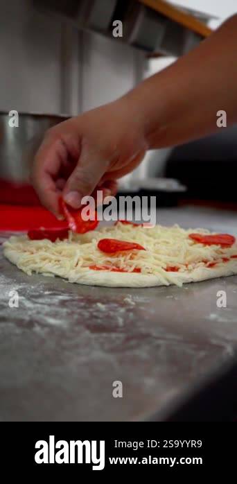 Chef places pepperoni slices on a pizza dough already covered with ...