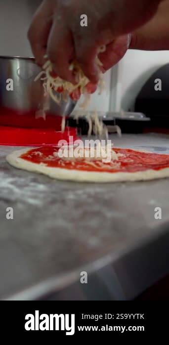 Hands spread shredded mozzarella cheese evenly over fresh pizza dough ...
