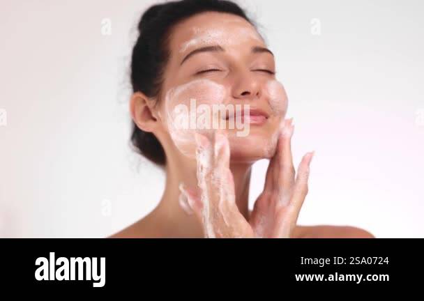 Radiant woman cleansing her face with a foamy cleanser, smiling during ...
