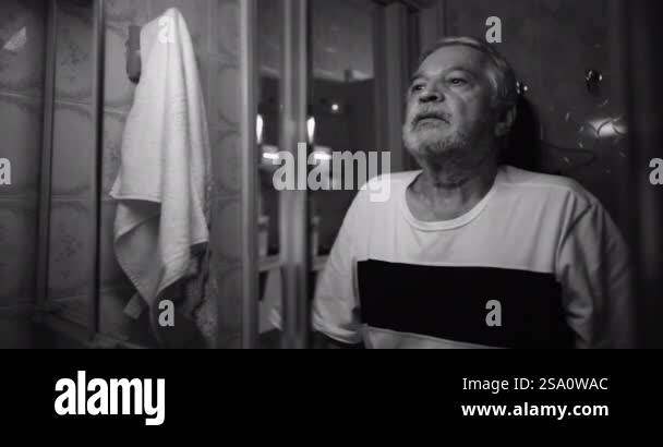 Elderly man staring at his own reflection in a bathroom mirror, lost in deep anguish and inner ...