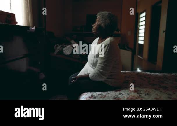 Lonely South American elderly lady sitting by bedside with peace ...