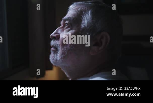 Man sitting on bed facing window indoors reflecting in solitude ...