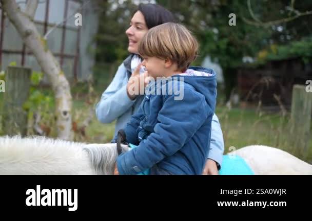 Child rides pony horseback, smiling mother and little boy son during ...