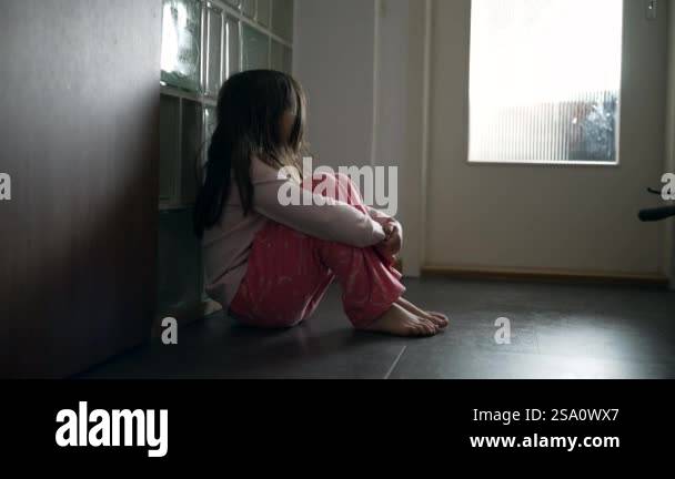 Sad child suffering from depression sitting alone in corridor feeling loneliness. Scared fearful ...