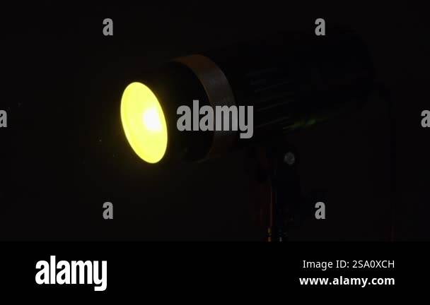 A studio spotlight emits a strong yellow light in a dark environment ...