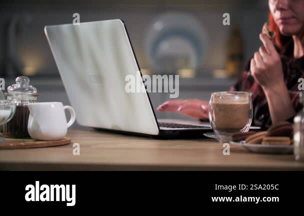 woman eating cookies and drinking coffee sitting at kitchen table in ...