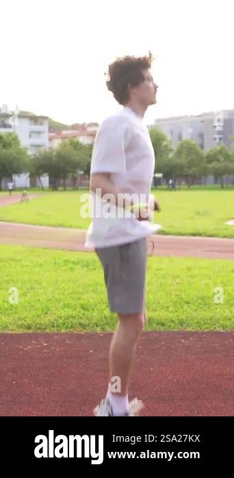 Vertical full length video of a caucasian young man warming up skipping ...