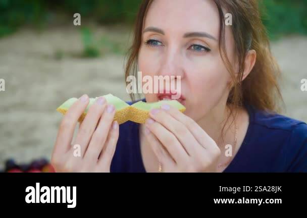 Woman eating melon with focused expression and relaxed demeanor. Female ...