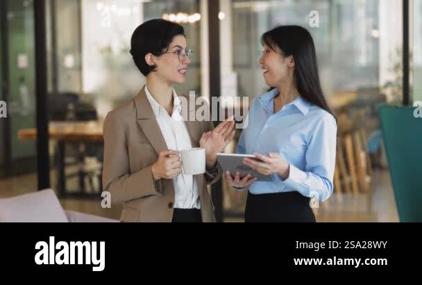 Two young friendly attractive women workmates met in office lobby, blab ...