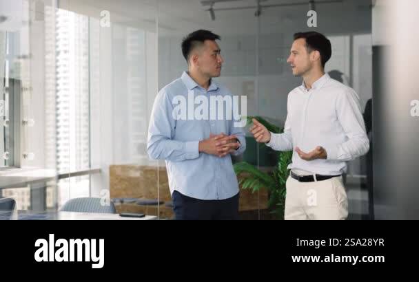 Two Latin and Asian male corporate friends talking in office space ...