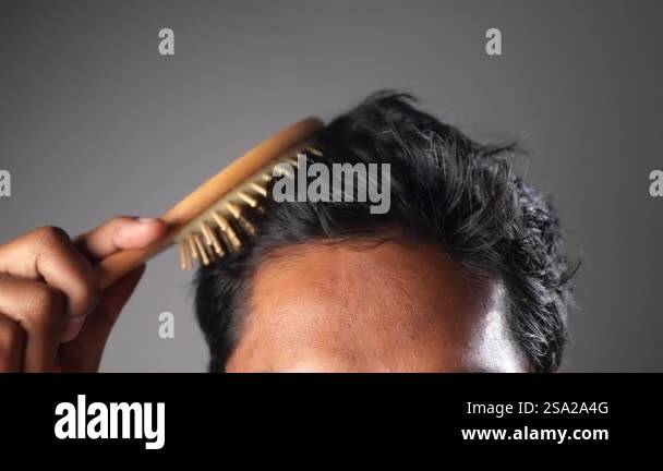 A man is brushing his dark hair with a wooden comb. The focus is on the ...