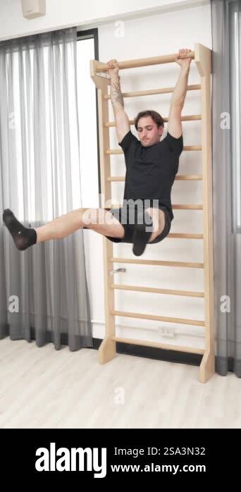 Happy man doing hanging leg raise exercise on wall bars to strengthen ...