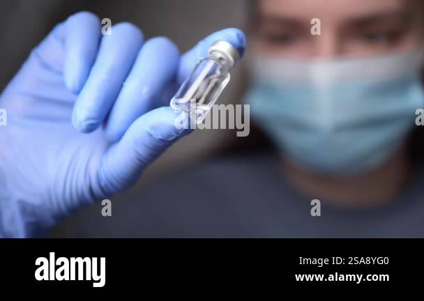 Female doctor in blue surgical mask and gloves shaking glass vial ...