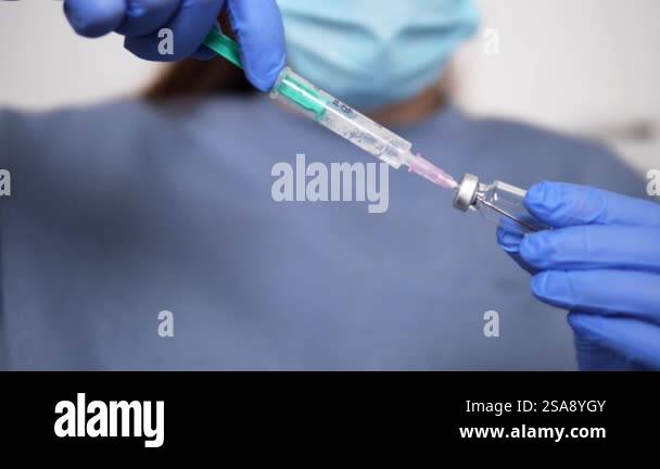 Doctor wearing blue gloves and surgical mask carefully filling syringe ...