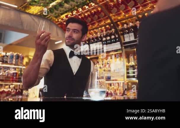 Focusing on smiling smart bartender preparing drinks at luxurious bar while engaging lively ...