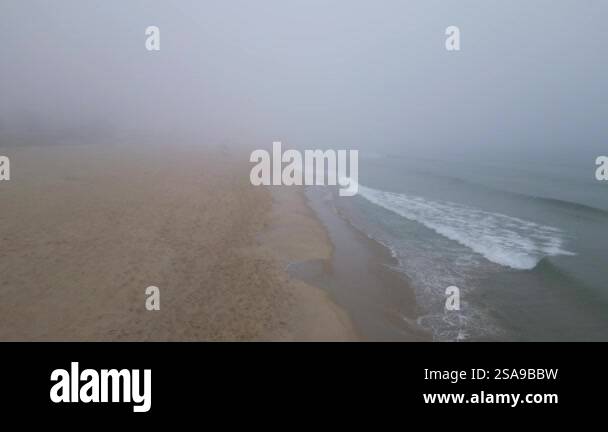 A foggy beach with soft sand and gentle waves meeting the shoreline ...