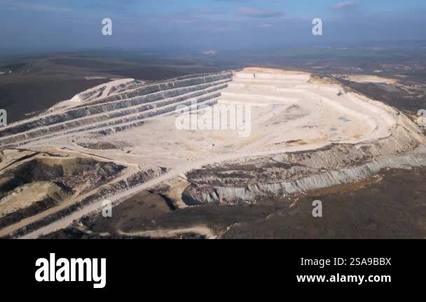 An open-pit quarry with terraced layers and heavy machinery operating ...