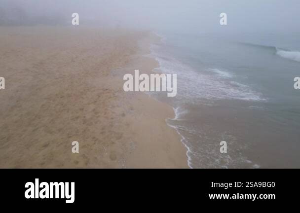 A foggy beach with soft sand and gentle waves meeting the shoreline ...