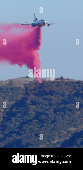 A firefighting aircraft propels bright pink fire retardant over the ...