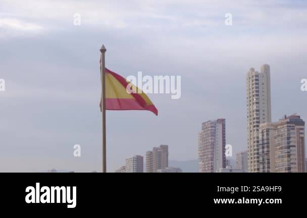 Spanish flag waving gracefully against a bright blue sky in Benidorm. A ...