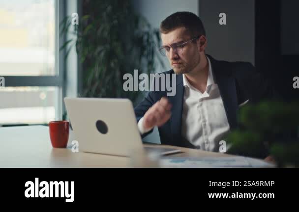 Focused businessman in a modern office working on a laptop, appearing ...