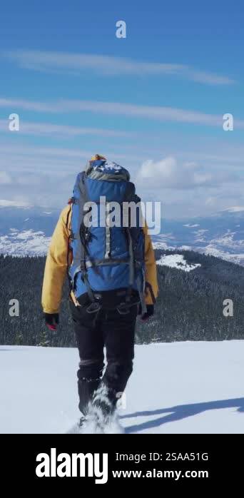 A hiker wearing a yellow jacket and blue backpack walks through deep ...