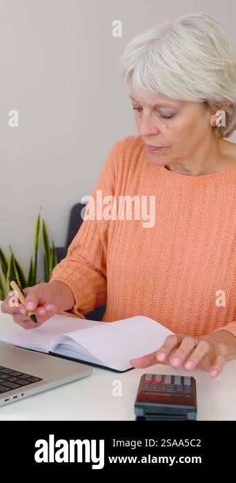 Senior woman using calculator and taking notes while managing home ...