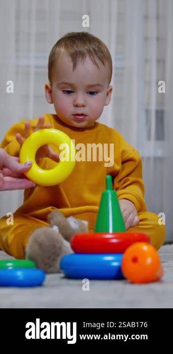 Mom's hand takes a piece of toy pyramid and gives it to her kid. Baby ...