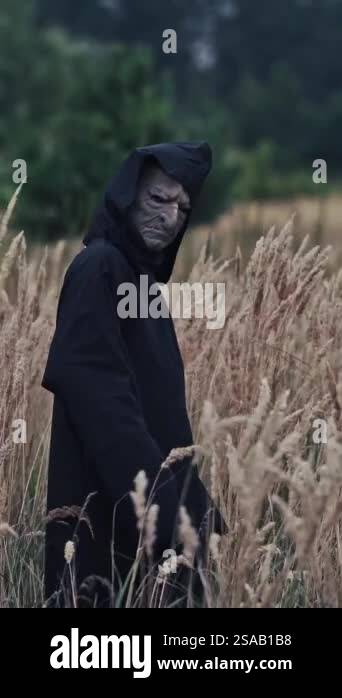 Scary black figure on a wheat field. Terrible ghost in dark mantle with ...