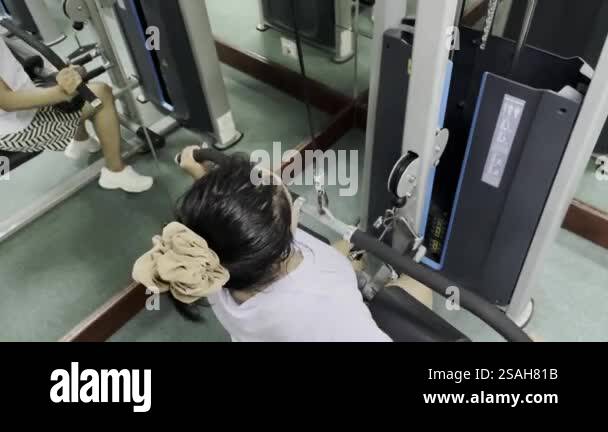 A woman is using the lat pulldown machine at the gym. She is pulling ...