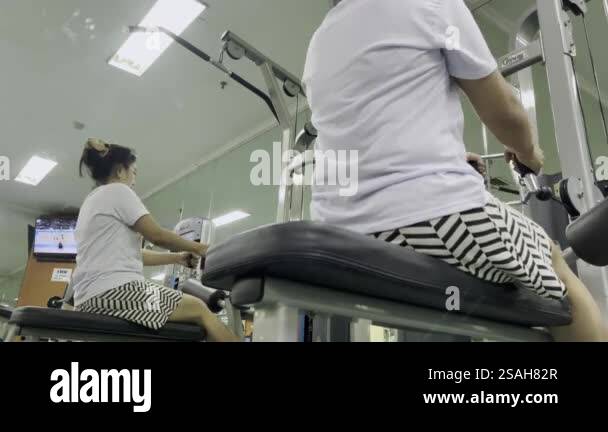 Two individuals are utilizing weight training machines in a gym setting ...