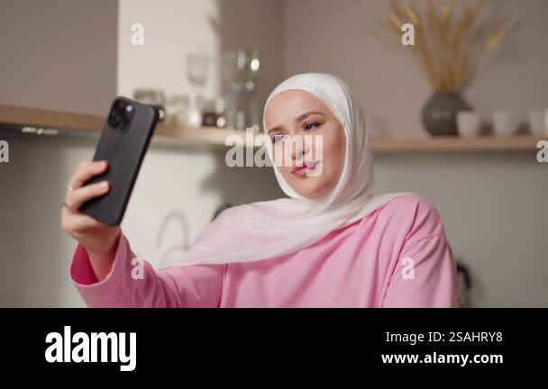 Muslim woman in white hijab expresses compassion during video call, her face showing concern and ...