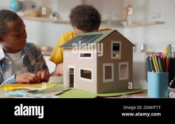 Close-up of cardboard house model with solar panels on roof as brothers ...