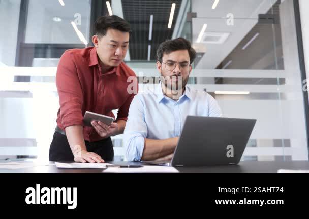 Two colleagues in office discussing project with laptop and tablet ...