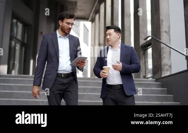 Two businessmen walk down the stairs outside modern office building ...