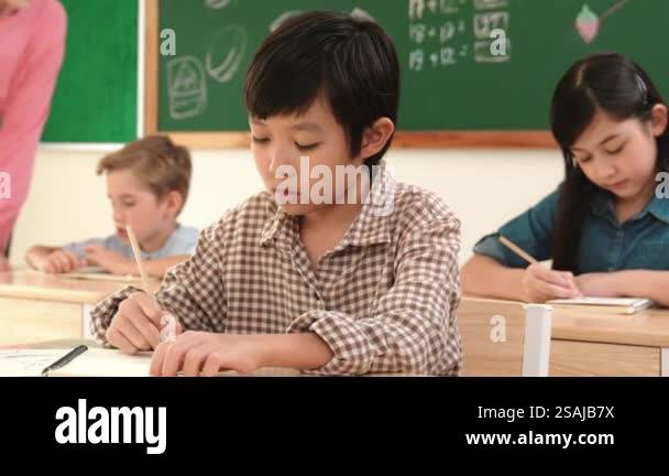 Asian smart boy smiling to camera while student writing answer in ...